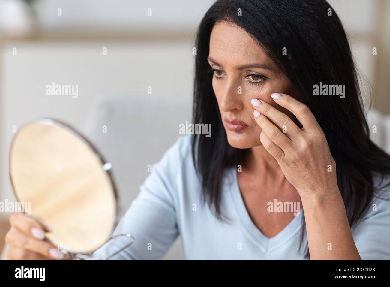 Adult woman checking her face in mirror, touching face Stock Photo - Alamy