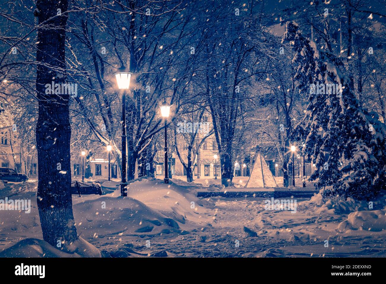Winter night park with lanterns, fountain, pavement and trees covered ...