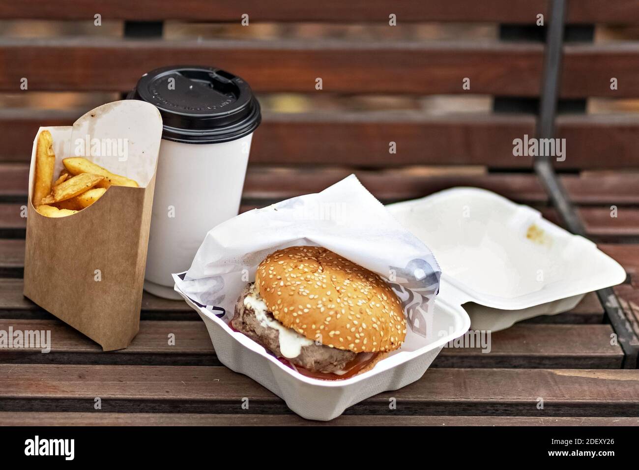 Fast food. Paper cups with coffee, hamburger boxes and fries on a park ...