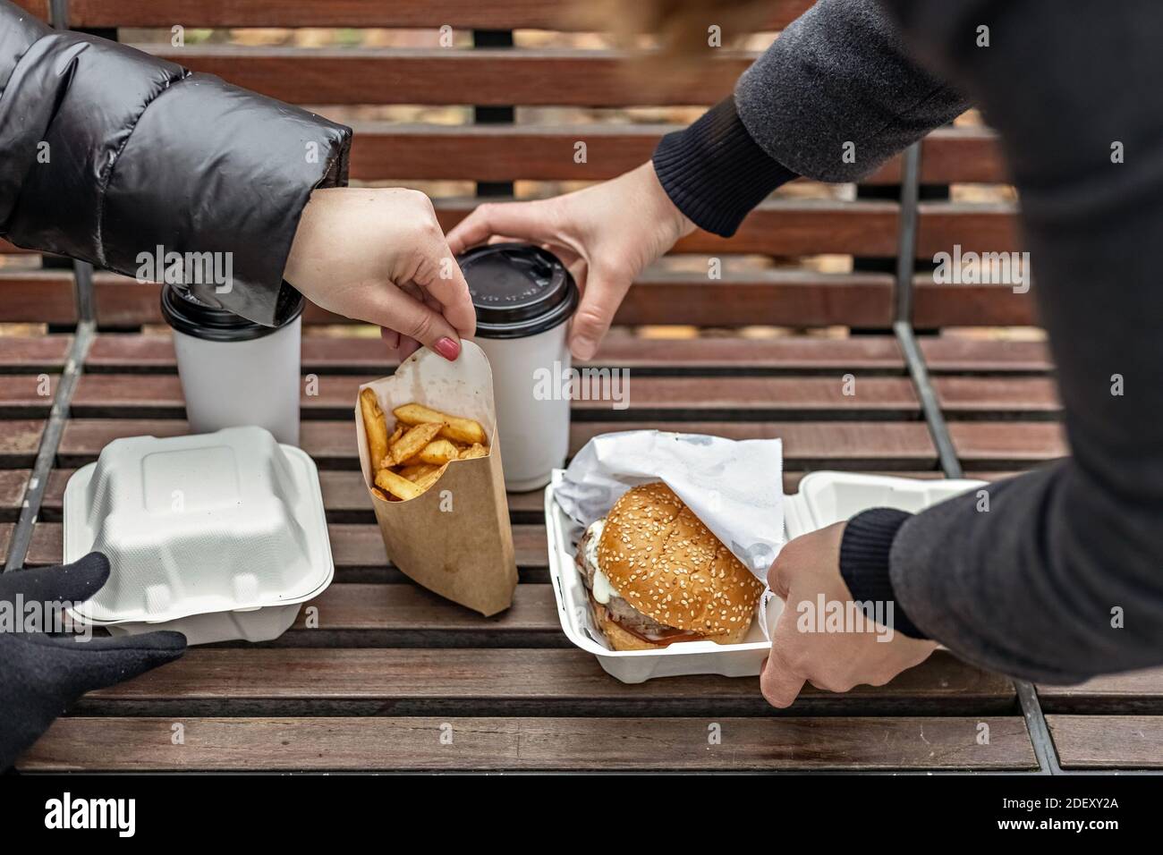Female hands lay out hamburgers with cups of coffee, fries on a park ...