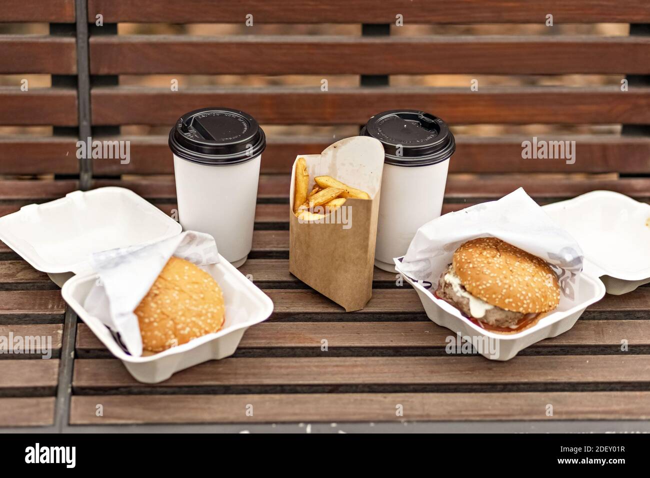 Fast food. Paper cups with coffee, hamburger boxes and fries on a park ...