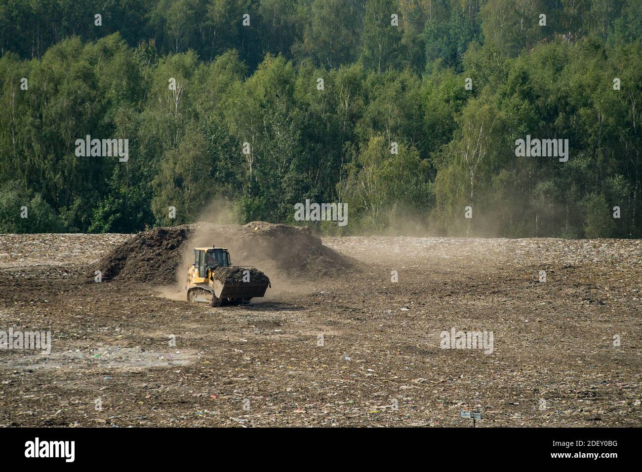 Yellow tractor loader works on huge landfill of big city. A lot of ...
