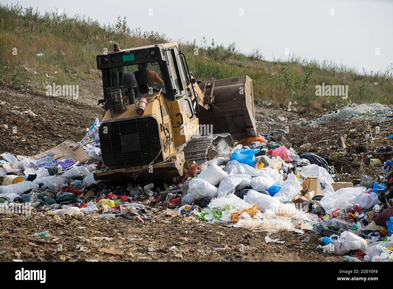 Yellow tractor on pile of household garbage. Waste sorting and ...