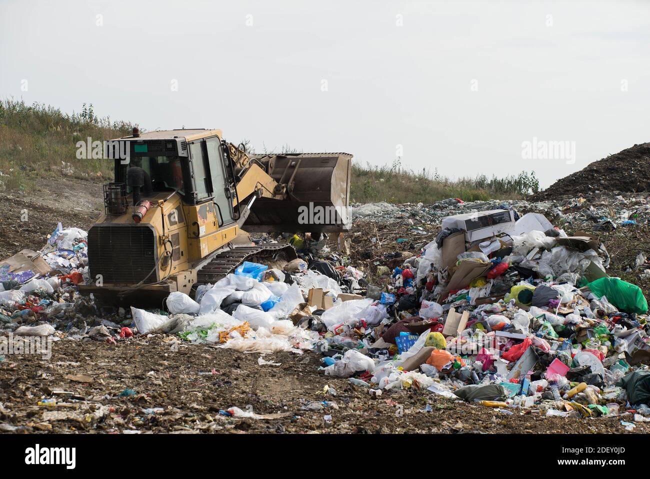 Huge dump of big city with different garbage. Yellow tractor unloading ...