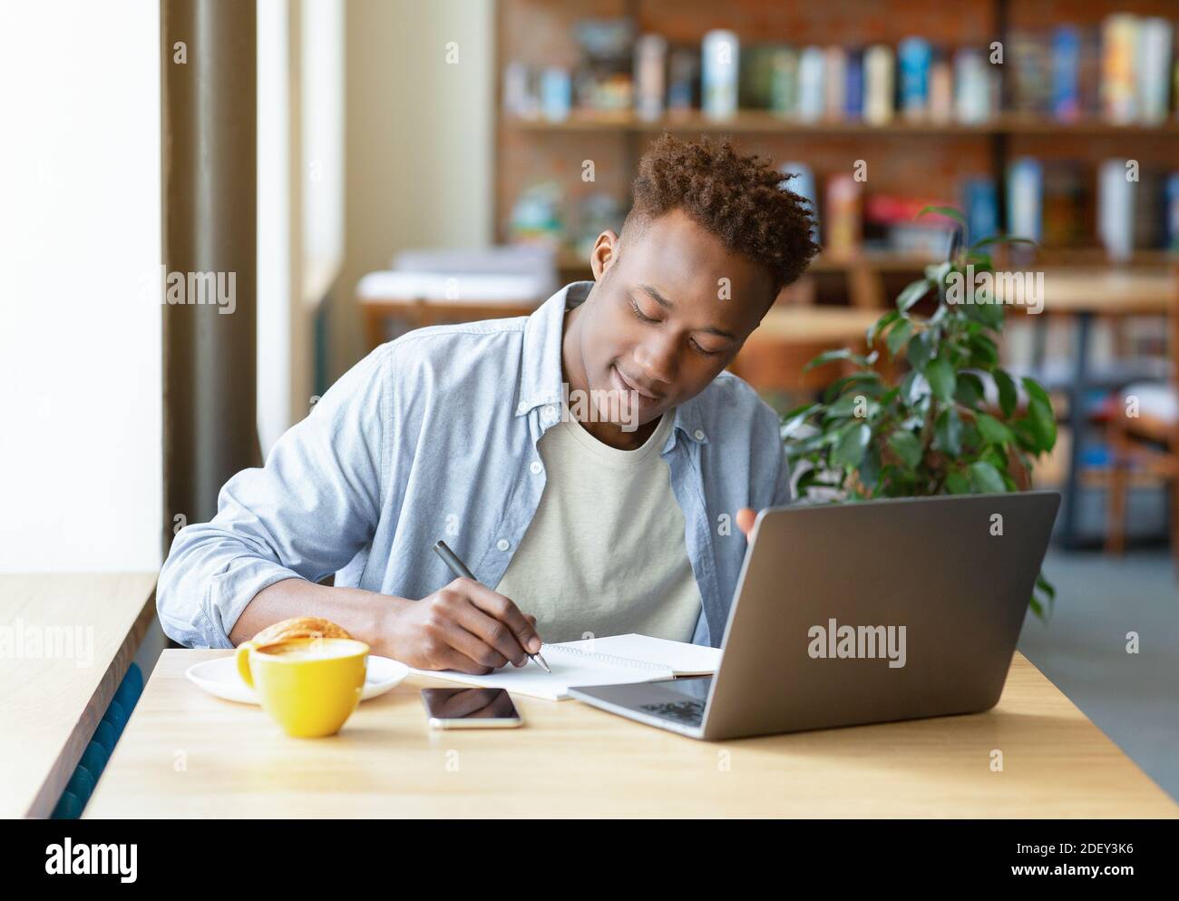 Positive black man using laptop for online work or studies, writing in ...