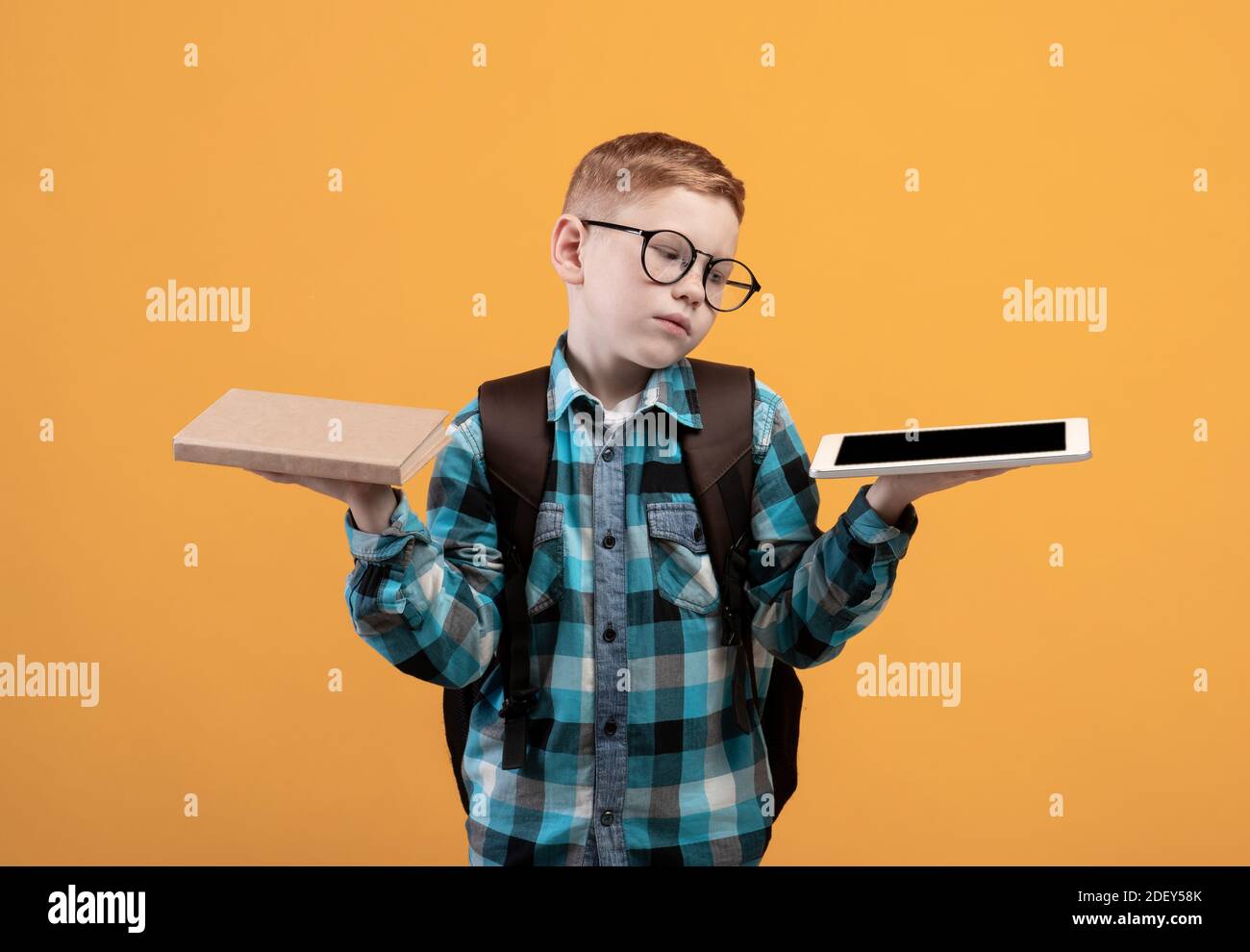 Confused schoolboy holding digital tablet and book Stock Photo - Alamy