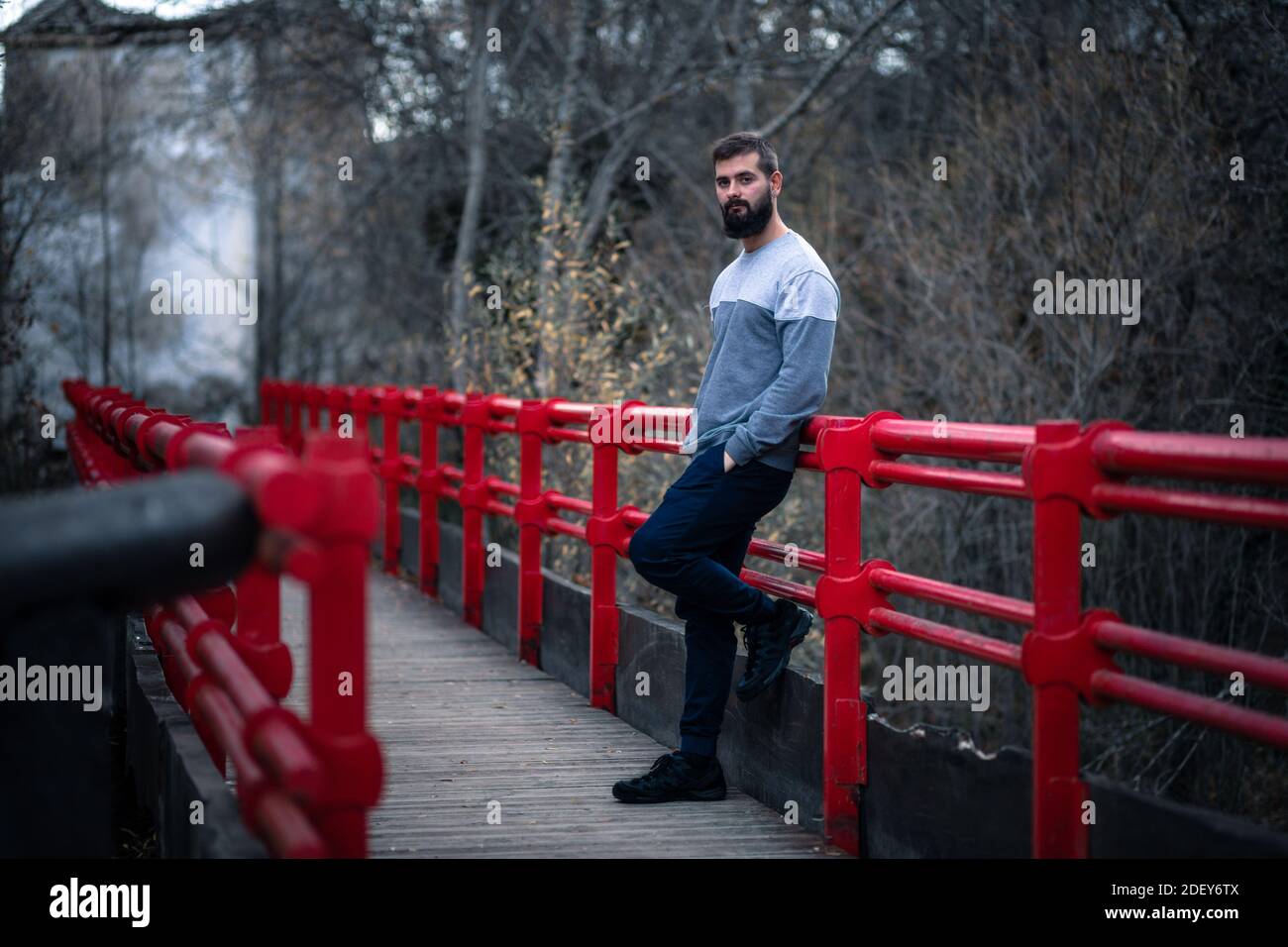 young handsome man leaning on the hand rail of a beautiful bridge with ...