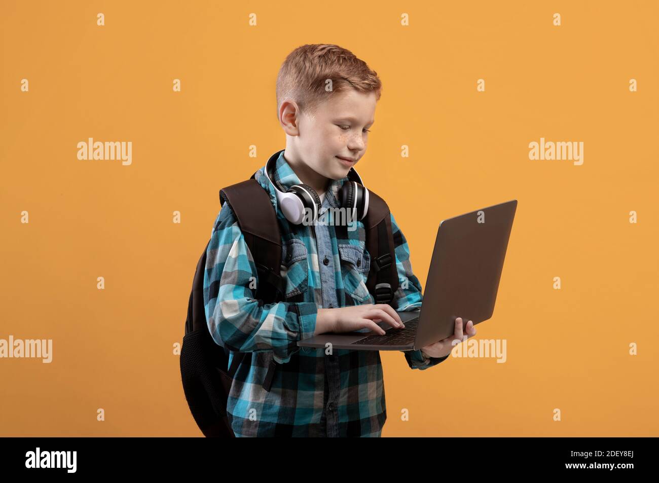 Smart schoolboy with backpack and headset holding laptop Stock Photo ...