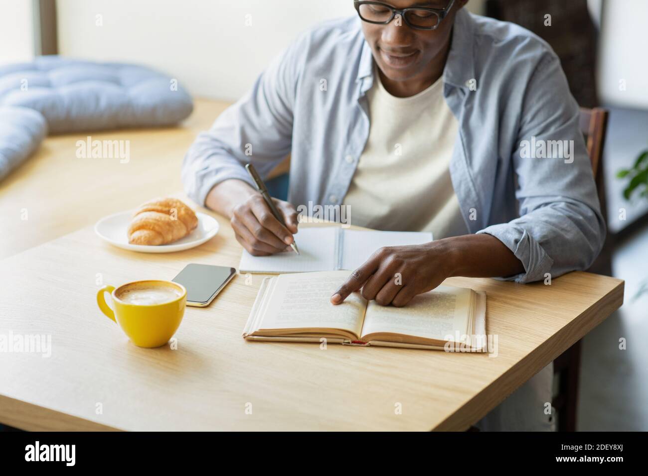 Cropped view of smart black guy taking notes from book at cafe ...