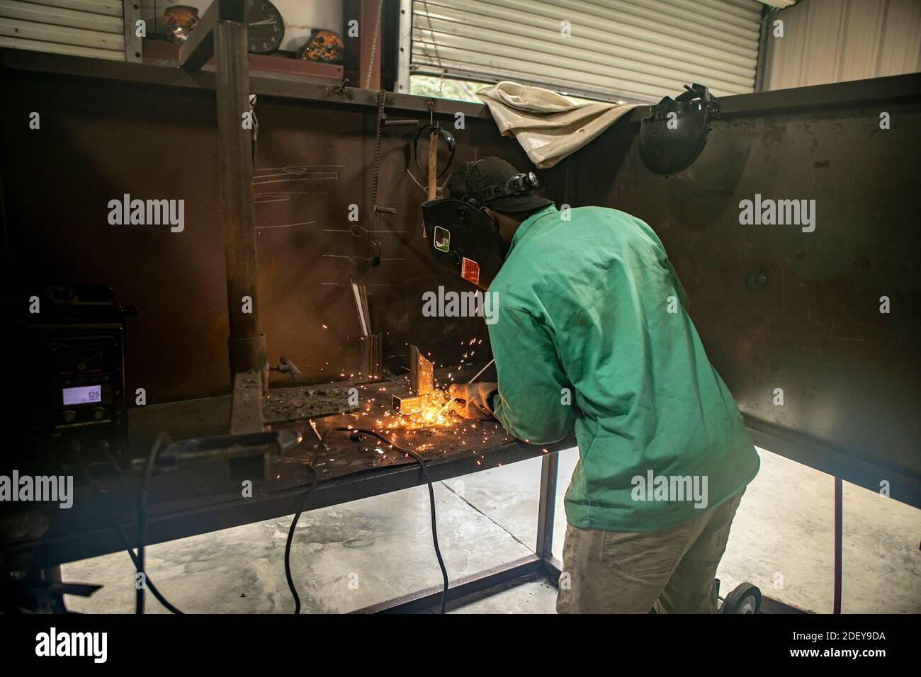 A man welds two pieces of metal together in a shop with an arc welder ...