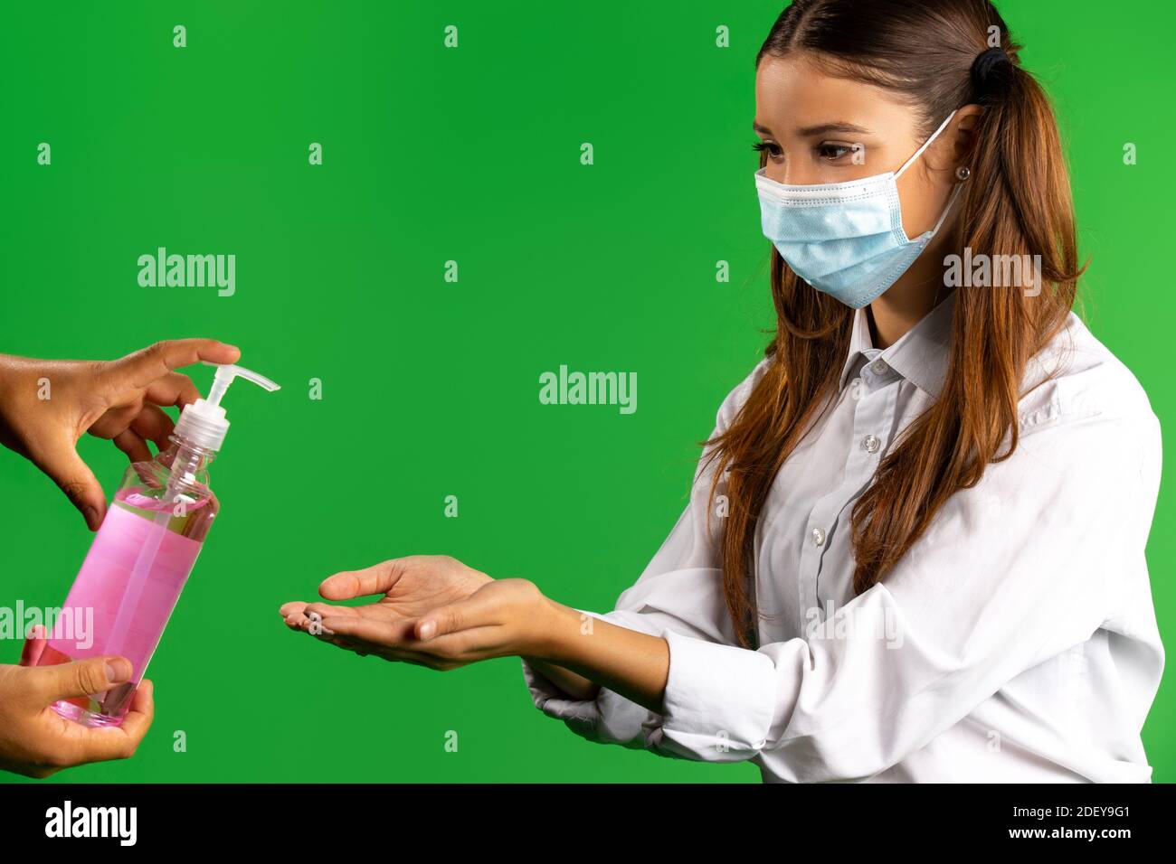 A brunette in a medical mask rubs hands with antiseptic before entering ...