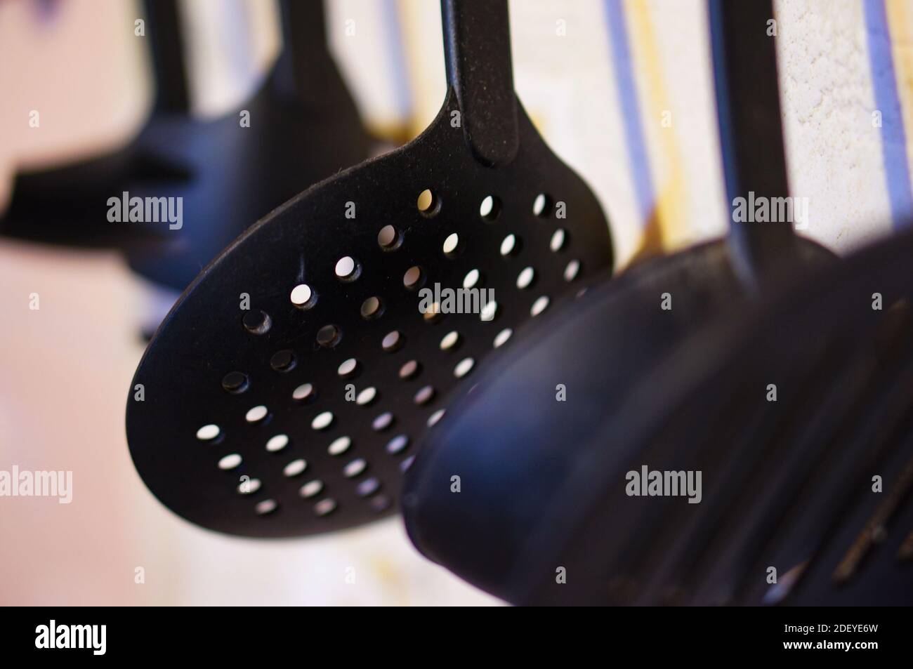 A closeup of a black plastic spatula with holes hanging in the kitchen ...
