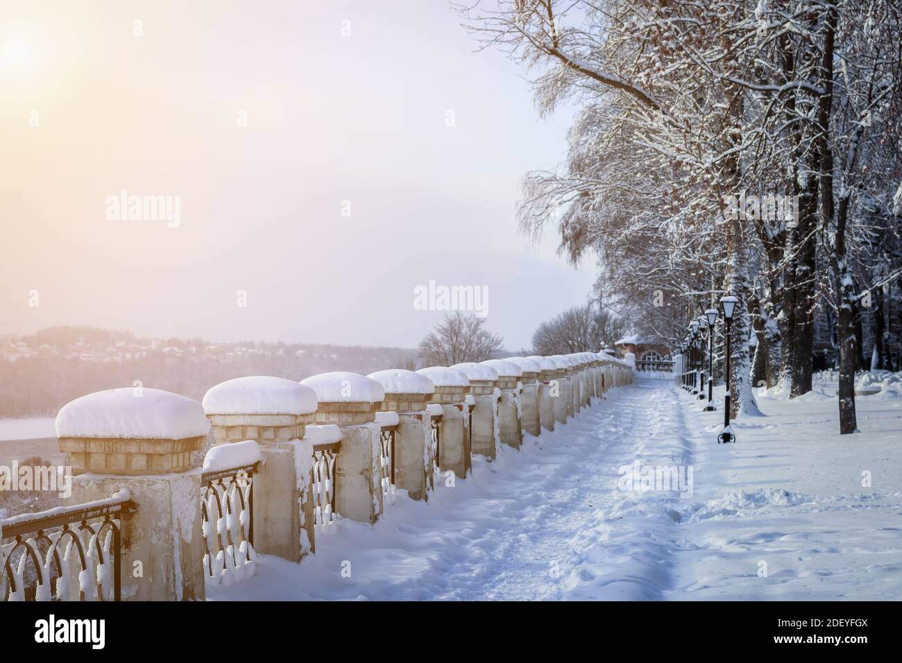 Sunset or sunrise in a winter park with trees, lanterns and a pavement ...