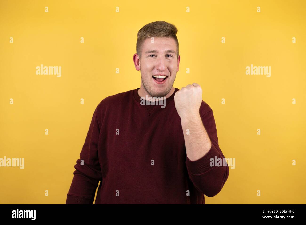 Young blonde man wearing a casual red sweater over yellow background ...