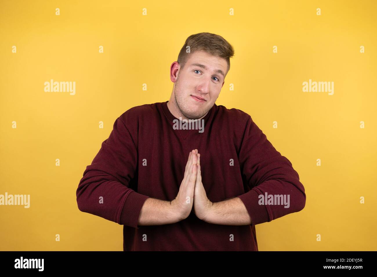 Young blonde man wearing a casual red sweater over yellow background ...