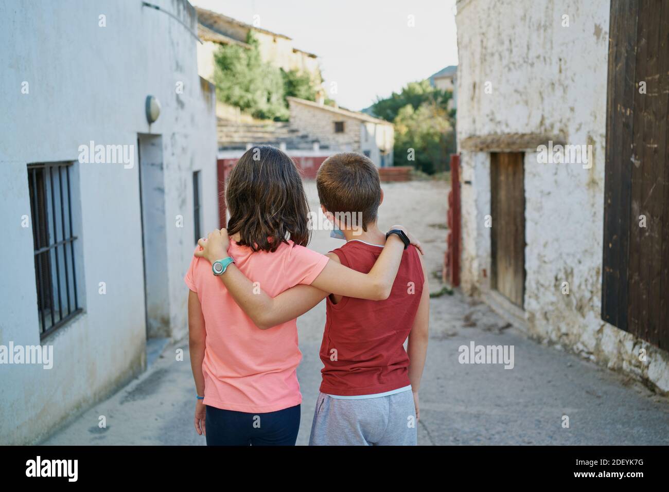 back view of kids walking embraced along the street in a Spanish ...