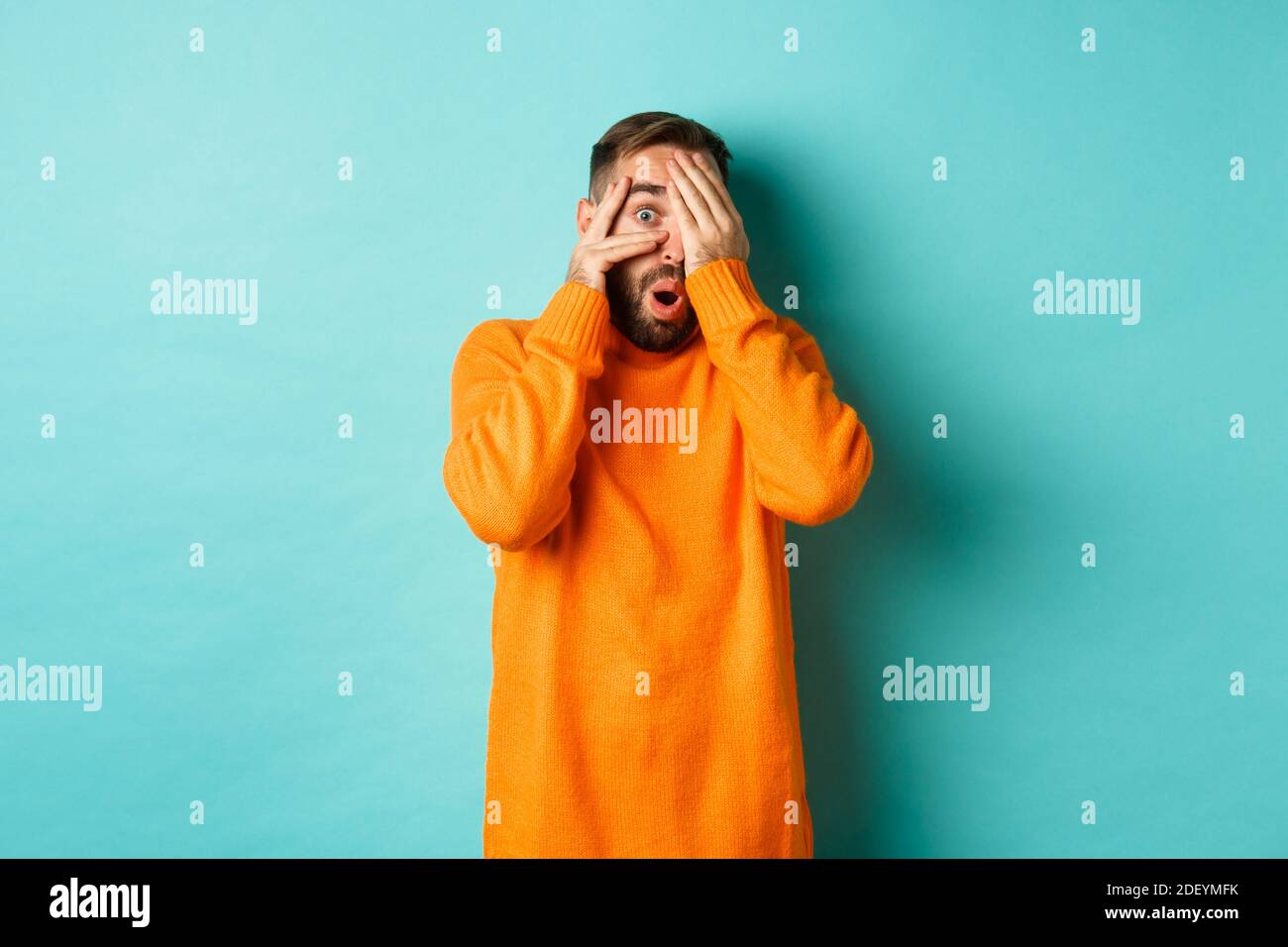 Curious man peeking at something, shut eyes but looking through fingers ...