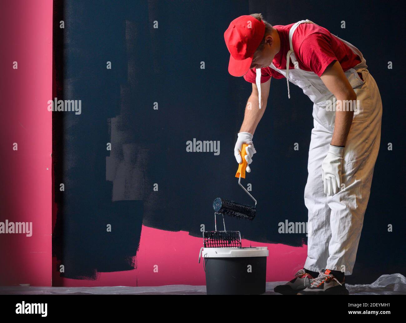 Man painting a wall. Painter in red overall painting wall in black ...