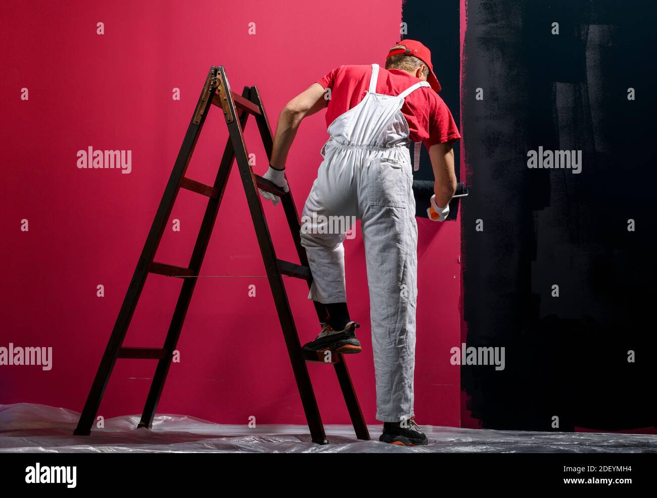 Man painting a wall. Painter in red overall painting wall in black ...