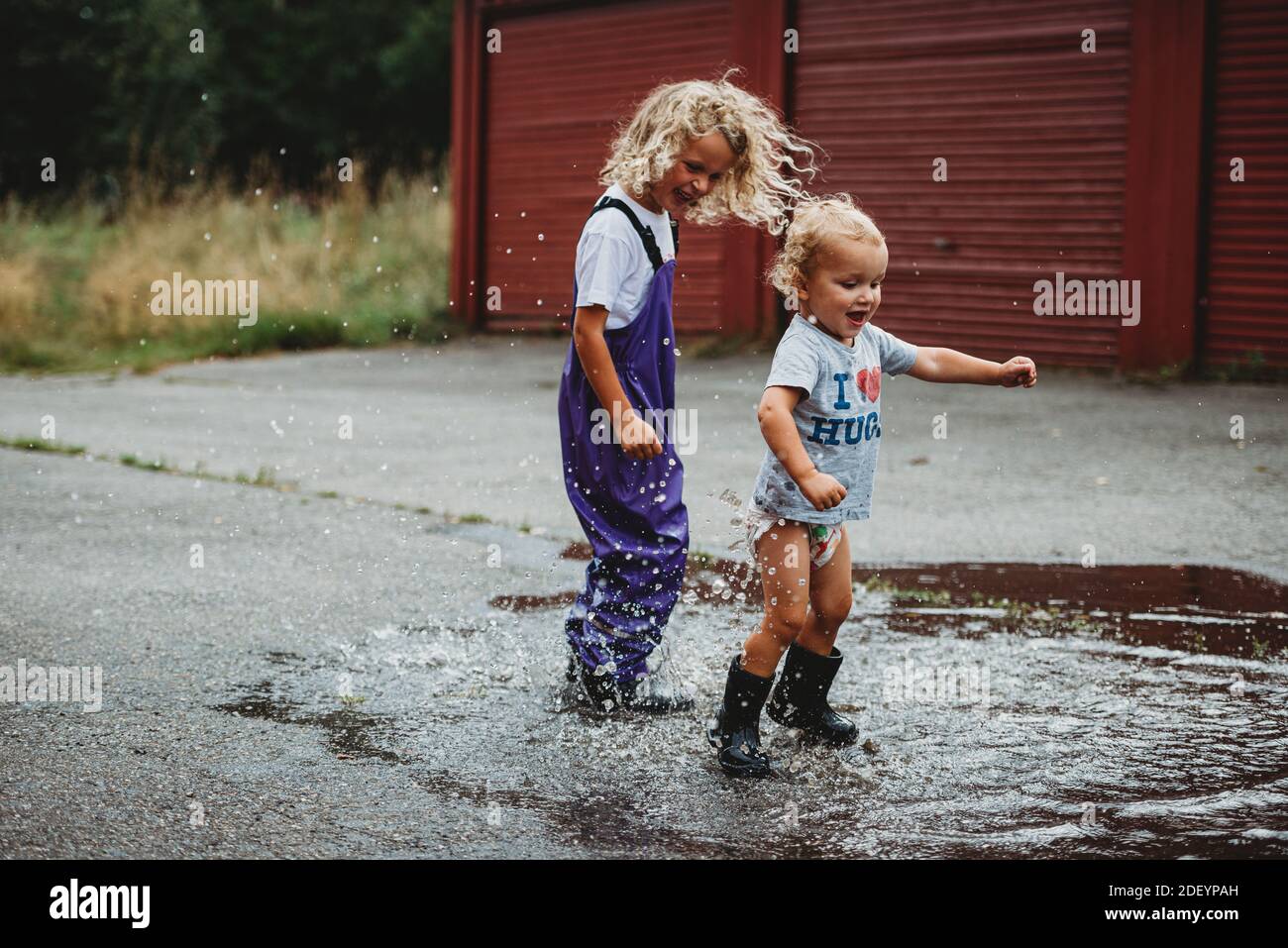 Siblings boy and girl jumping in a puddle having fun and smiling Stock ...