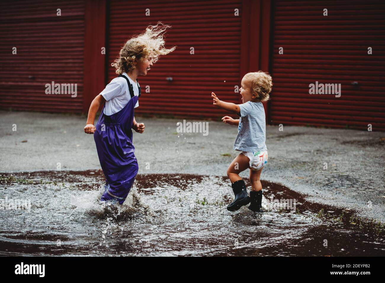 Siblings boy and girl jumping in a puddle having fun Stock Photo - Alamy