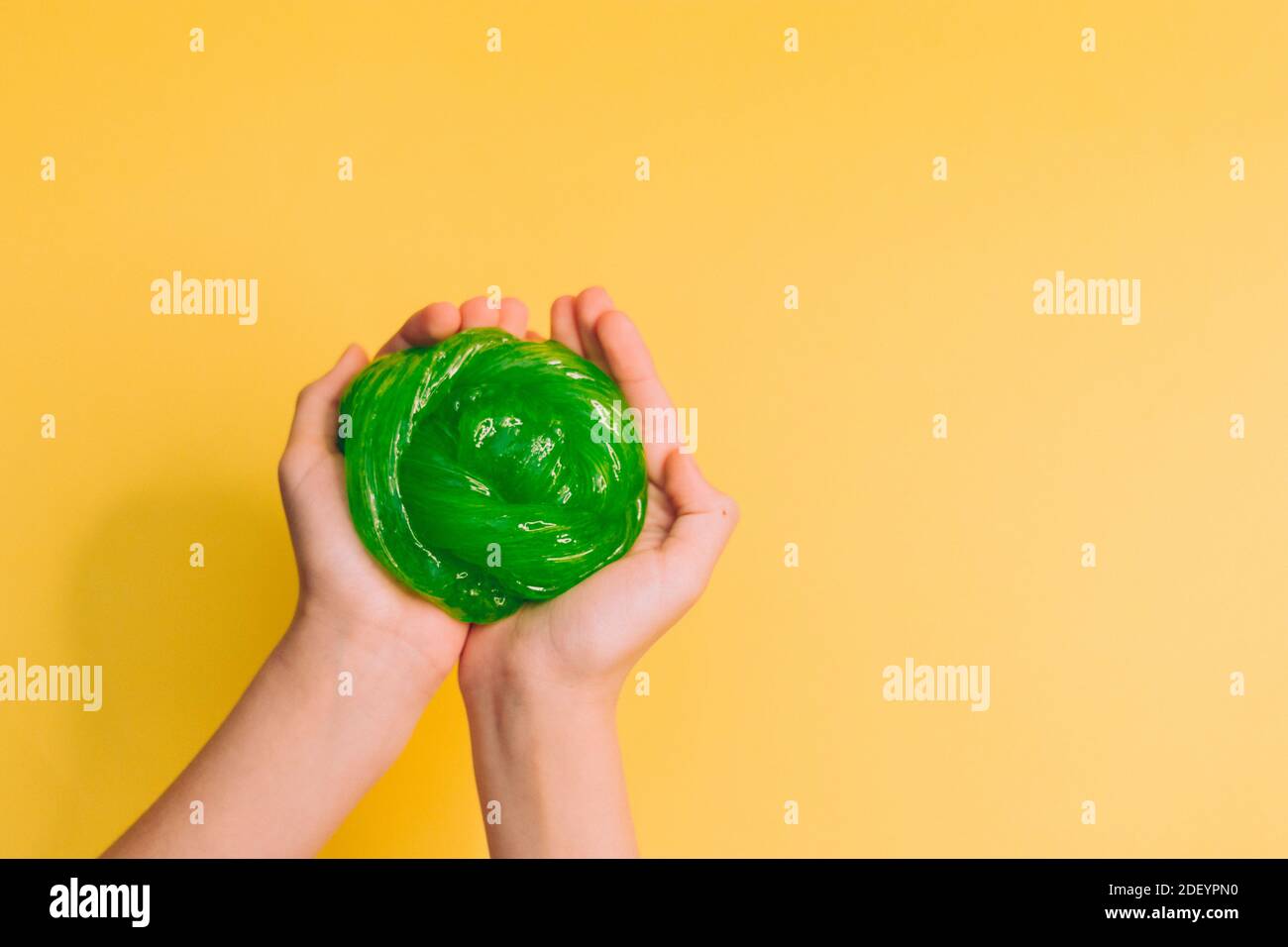 Make a slime green round slimy toy in the hands of children on a yellow ...