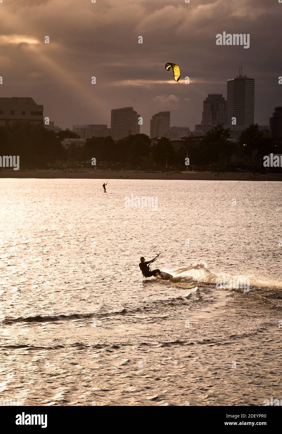 A woman kiteboarding on a summer evening with a dark Boston skyline ...
