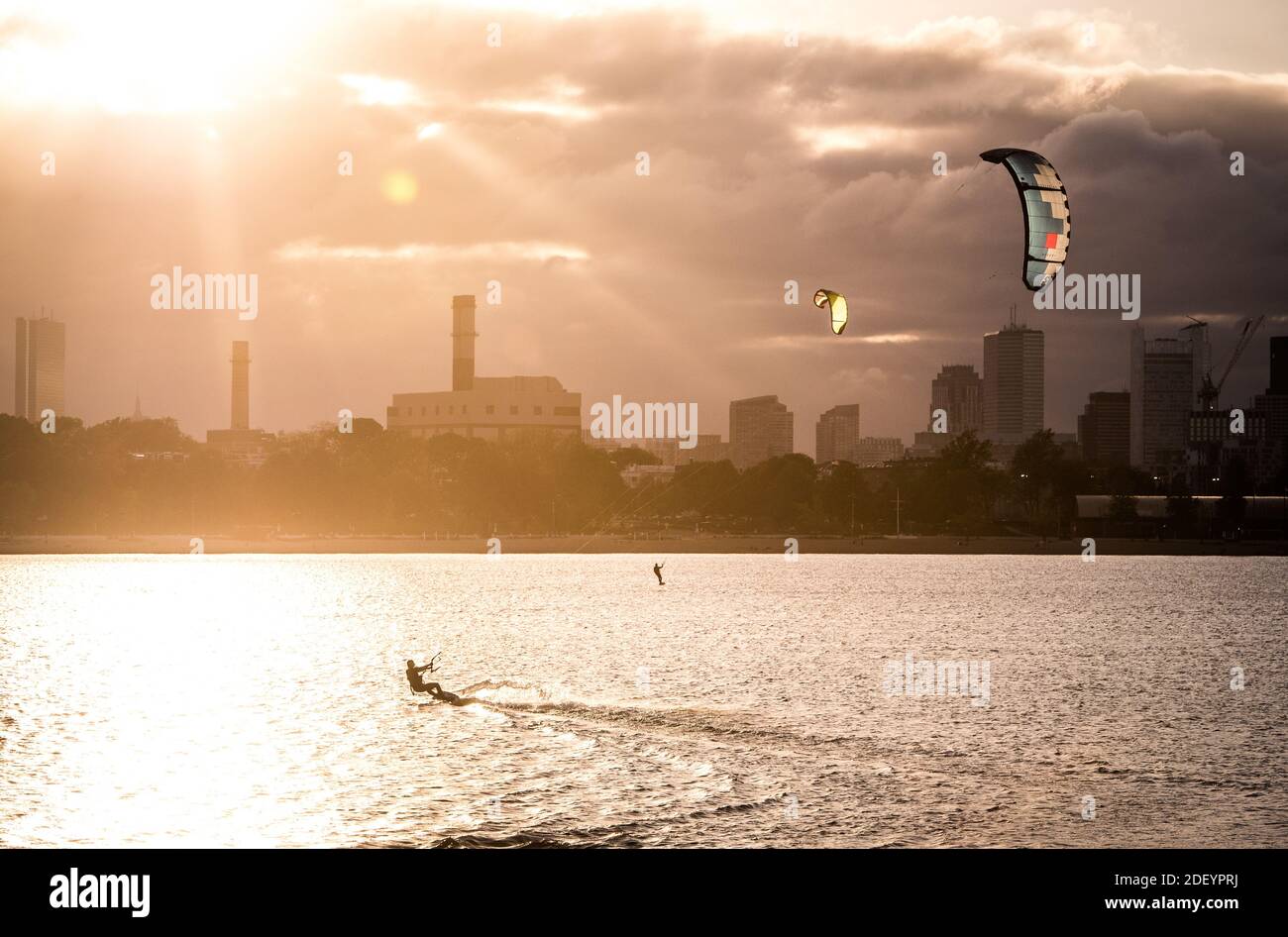 A woman kiteboarding on a summer evening with a dark Boston skyline ...