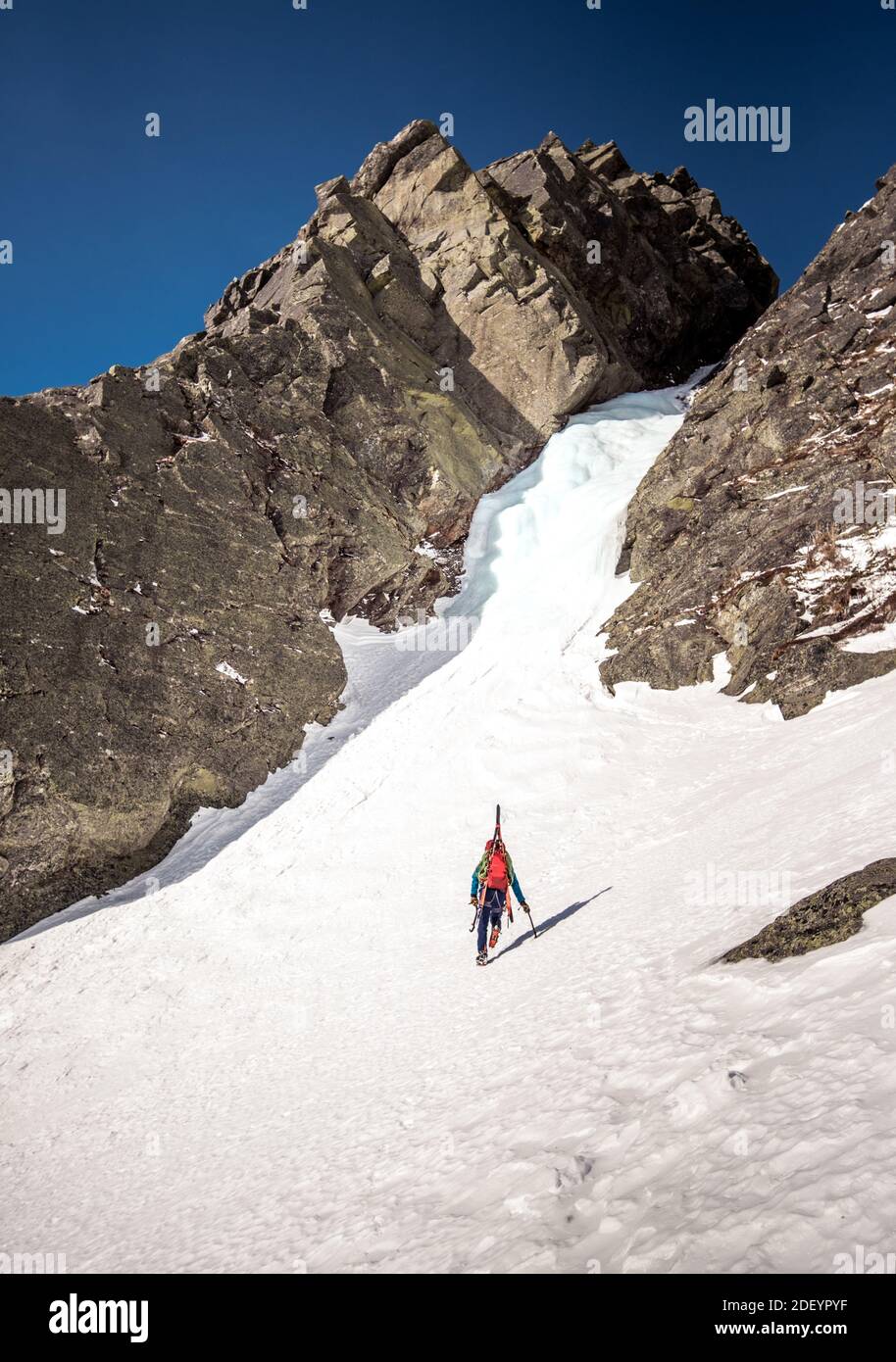 Ice climber walking towards ice gully with skis on back Stock Photo - Alamy
