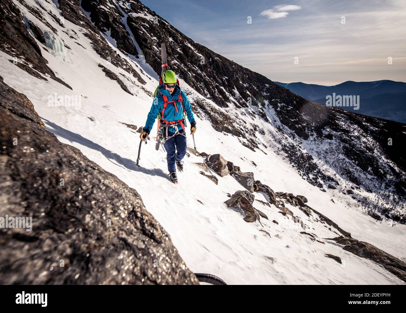 Climber walking through rocks on side of snowy mountain Stock Photo - Alamy