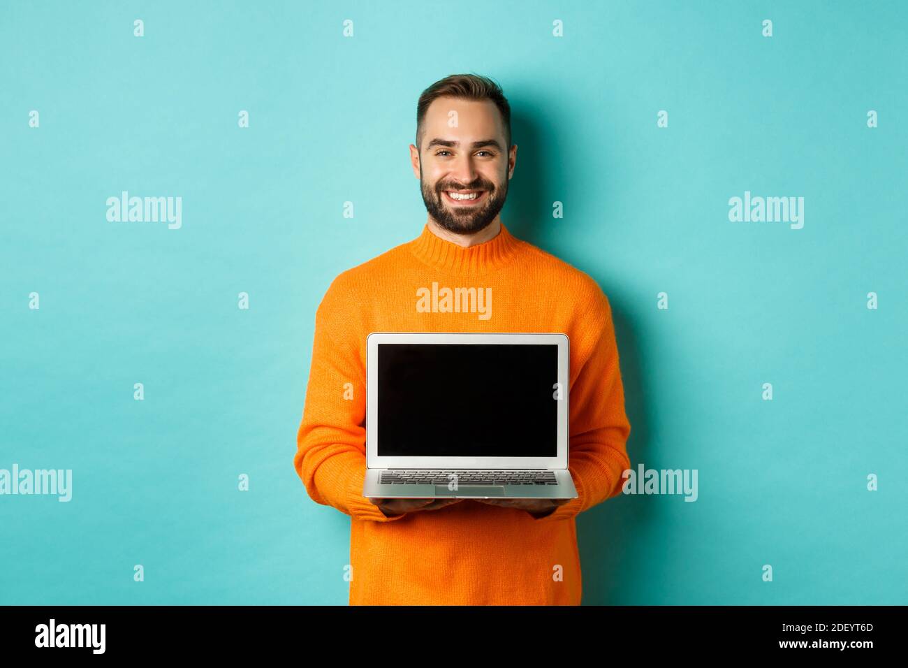 Handsome bearded man in orange sweater showing laptop screen ...