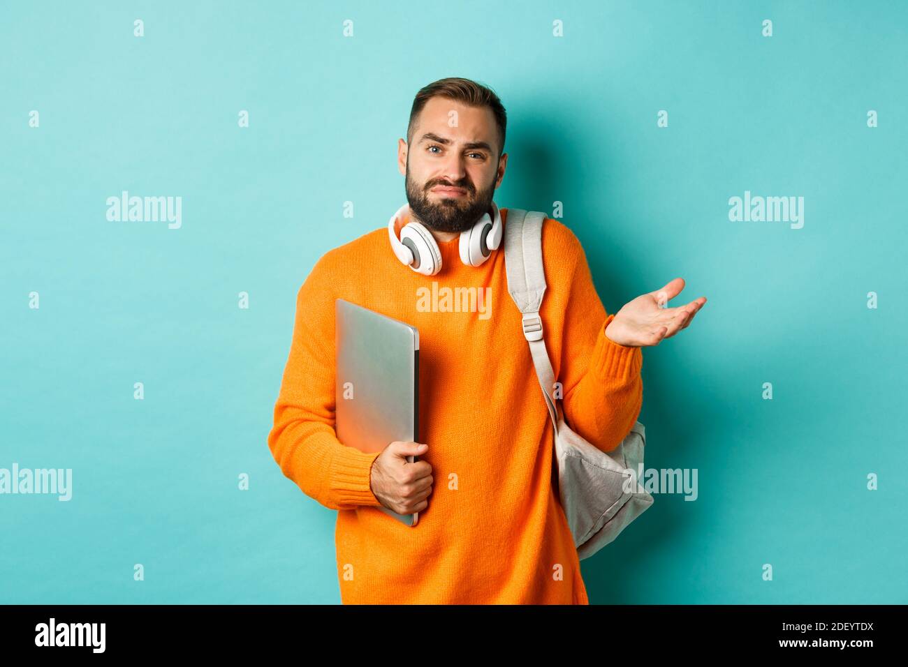 Image of troubled young man with headphones and backpack, shrugging ...