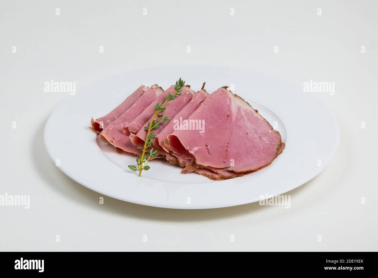 A plate of ham slices decorated with an oregano branch on the white ...
