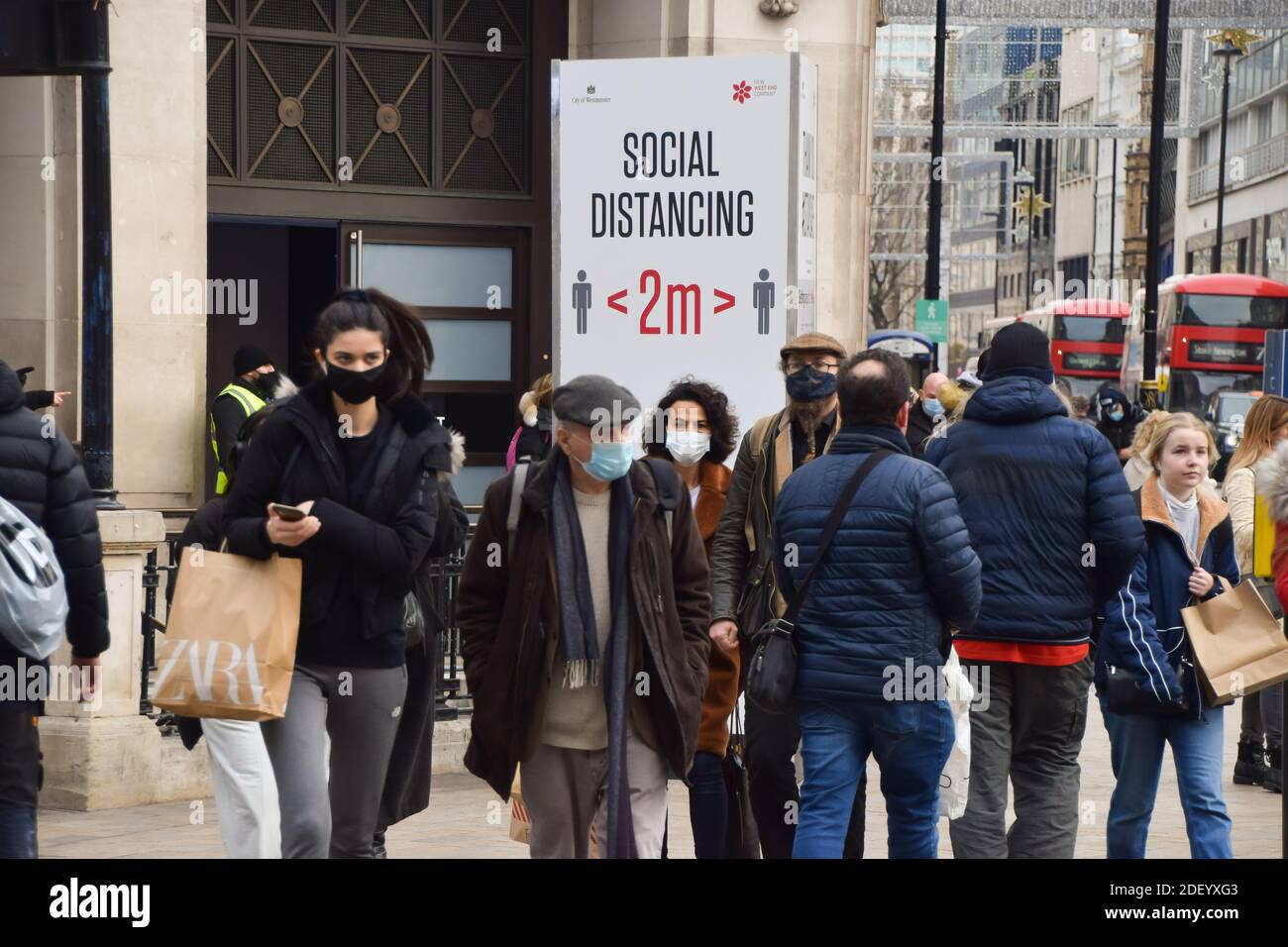 People wearing protective face mask walks past a Social Distancing sign ...