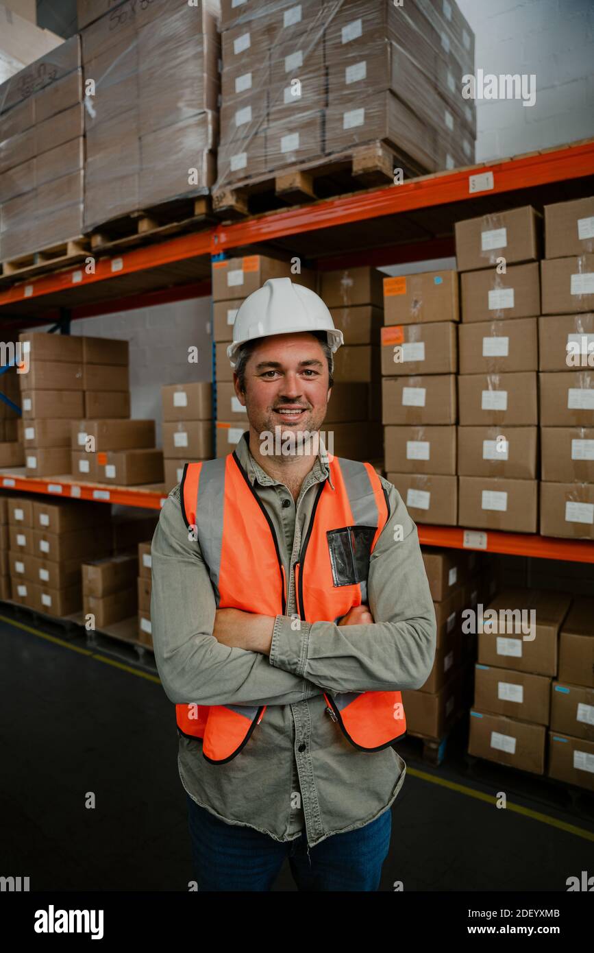 Smiling caucasian male worker standing cross-armed in front of parcels ...