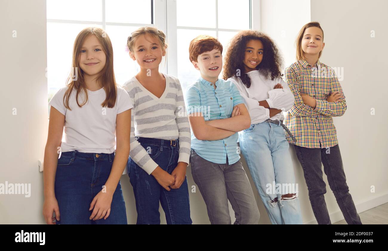 Smiling diverse children standing by the window at home or during break ...