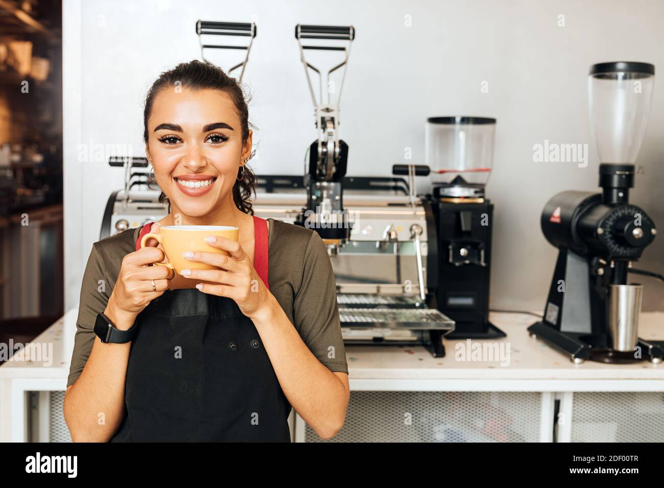 Beautiful cheerful barista holding a mug and looking at camera. Smiling ...
