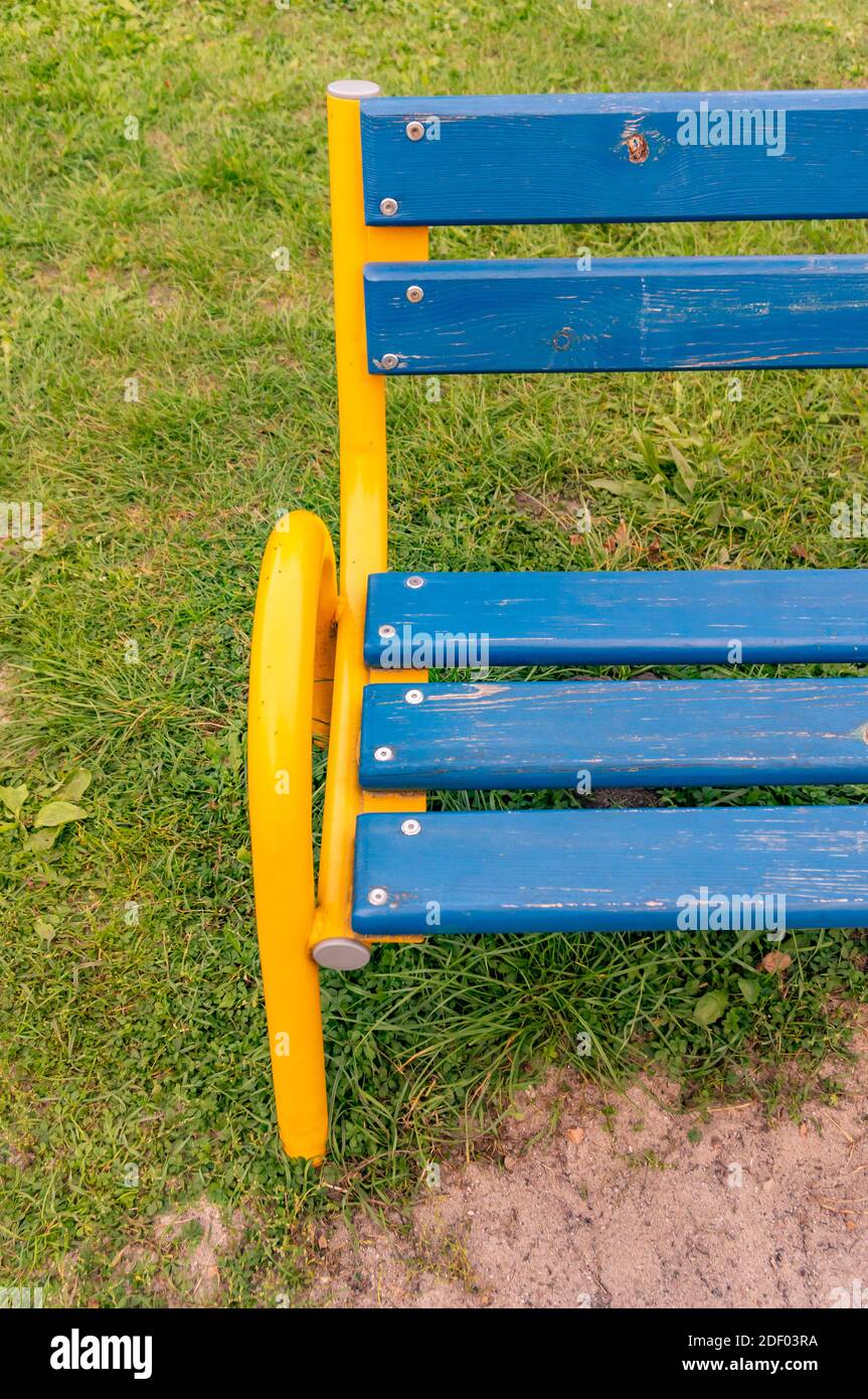 A vertical shot of a blue and yellow bench in a park under the sunlight ...