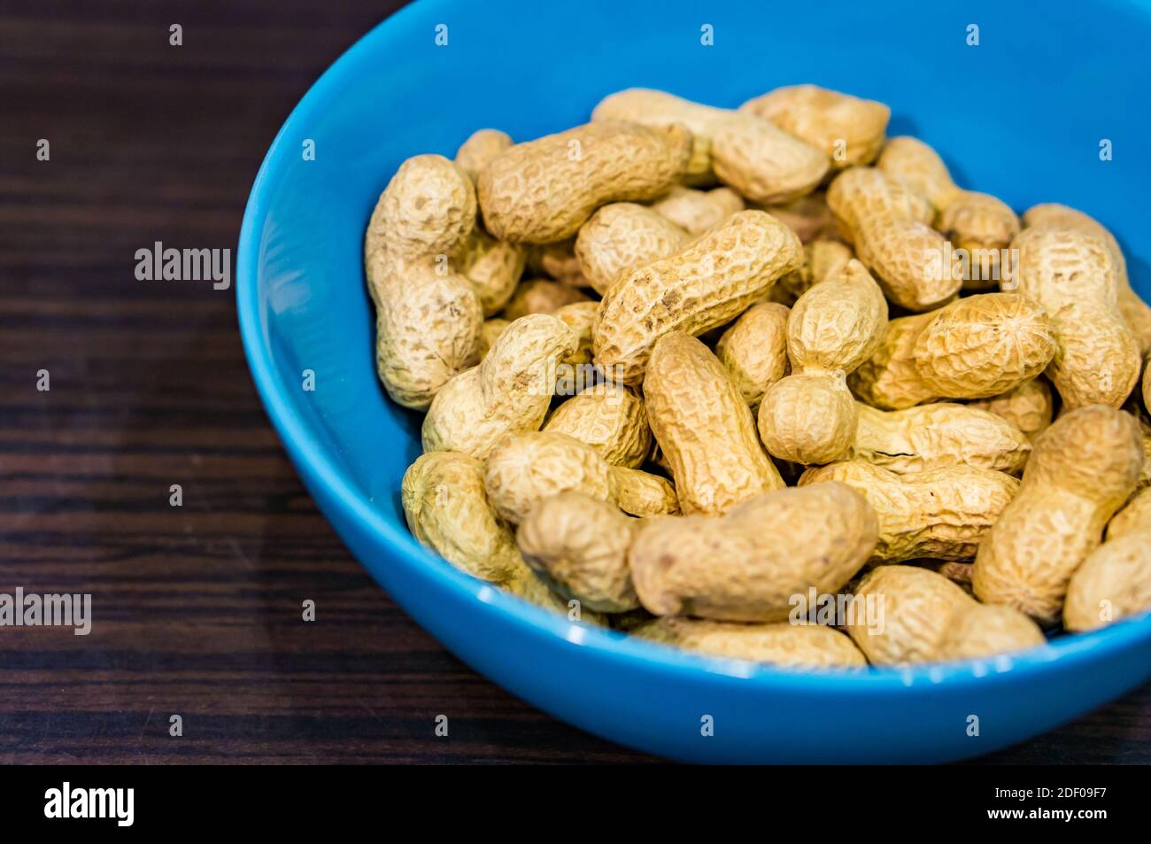 A closeup shot of peanuts in the blue bowl on a dark brown table Stock ...