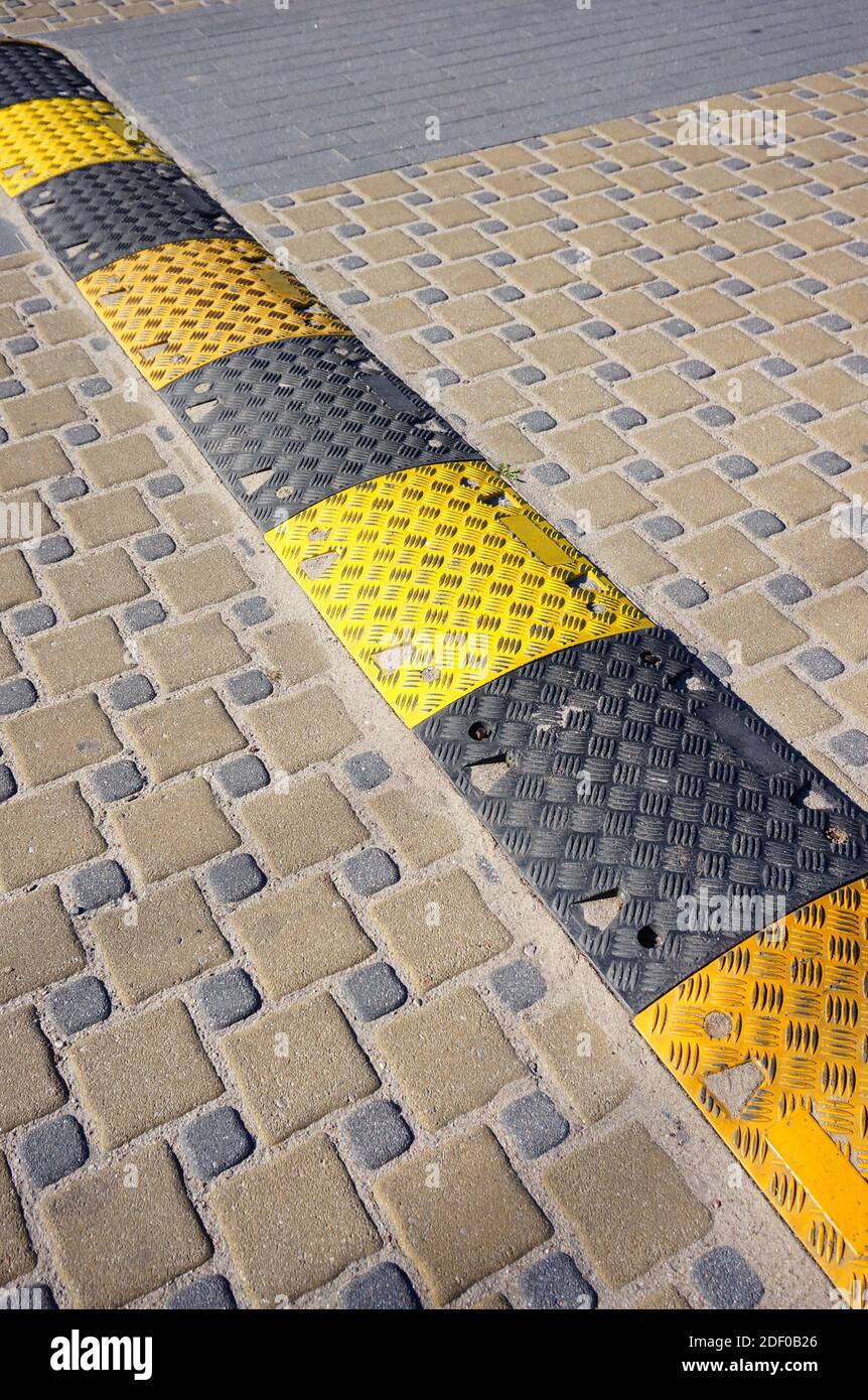 A yellow and black striped speed bump on cobblestone street Stock Photo ...