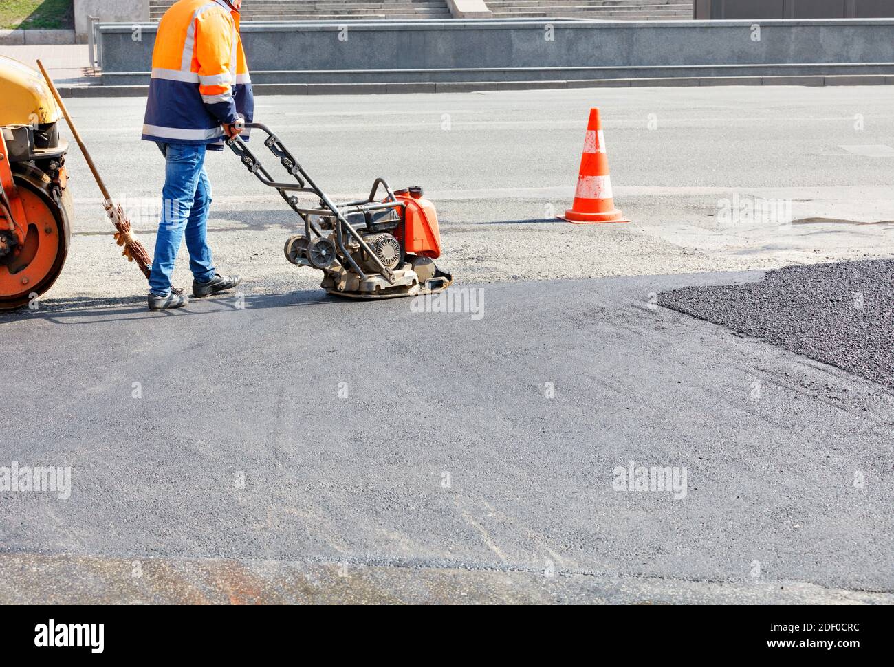A road worker compacts asphalt on a fenced road section of the roadway ...