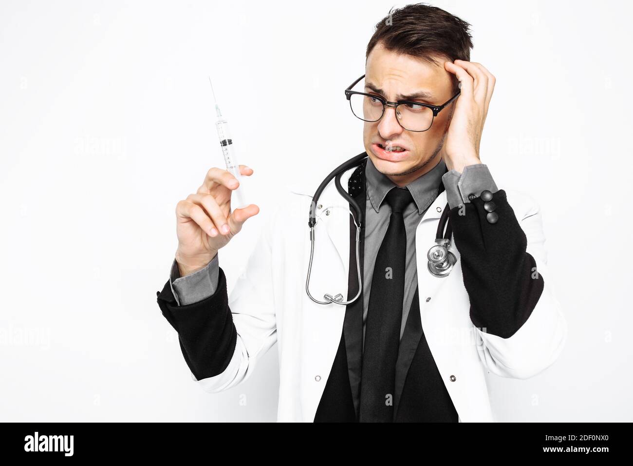 A tense doctor with a stethoscope on his neck, holding a syringe for ...