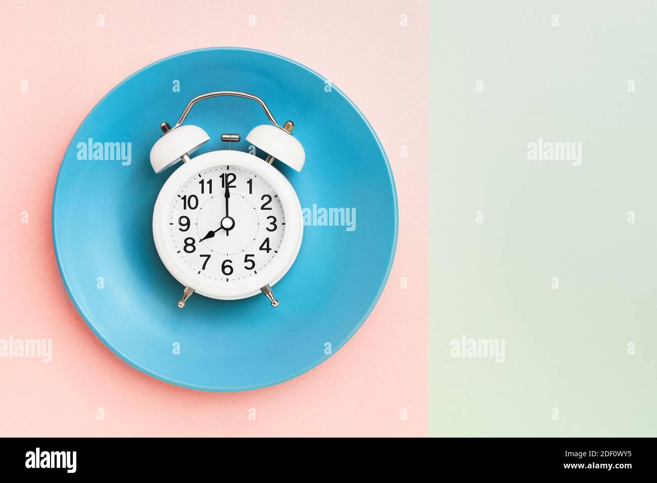 Intermittent fasting concept. White alarm clock on the empty blue plate ...