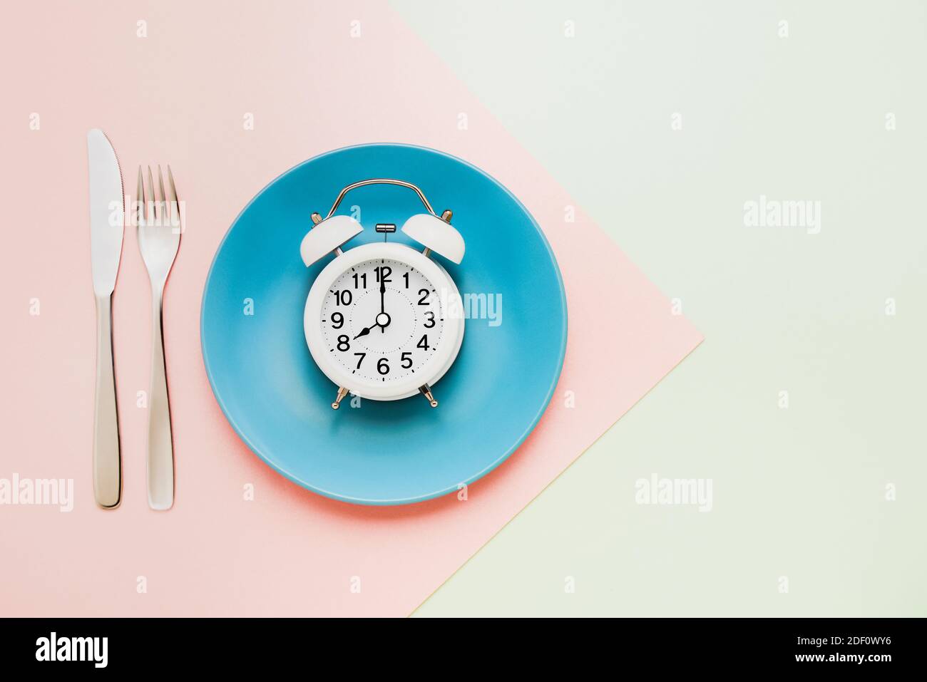Intermittent fasting concept. White alarm clock on empty blue plate ...
