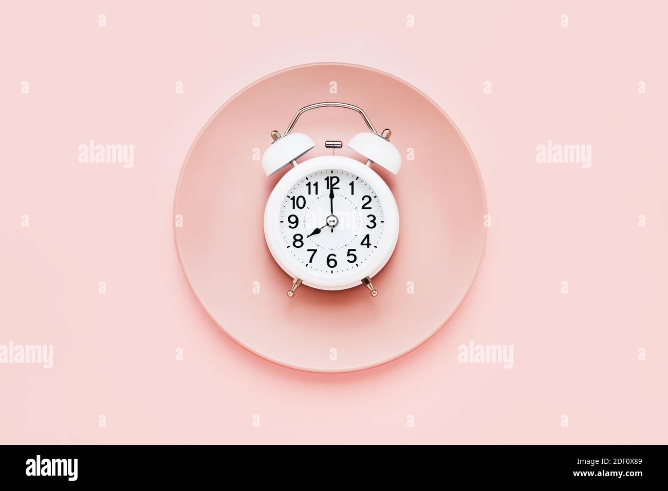 Intermittent fasting concept. White alarm clock on an empty pink plate ...