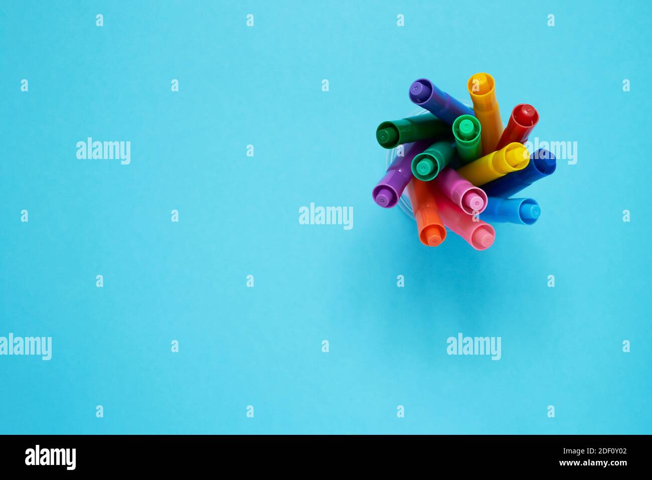 Set of markers in a cup and on light blue background. Top view. Back to ...