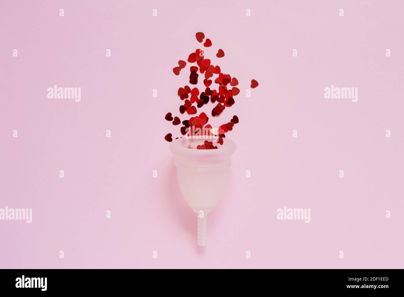 Reusable menstrual cup filled with red confetti on pink background ...