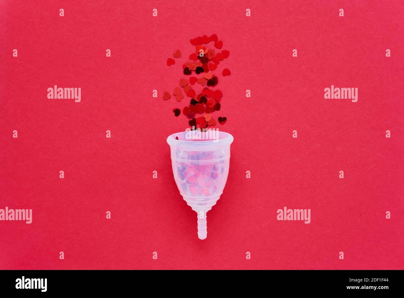 Reusable menstrual cup filled with red confetti on red background ...