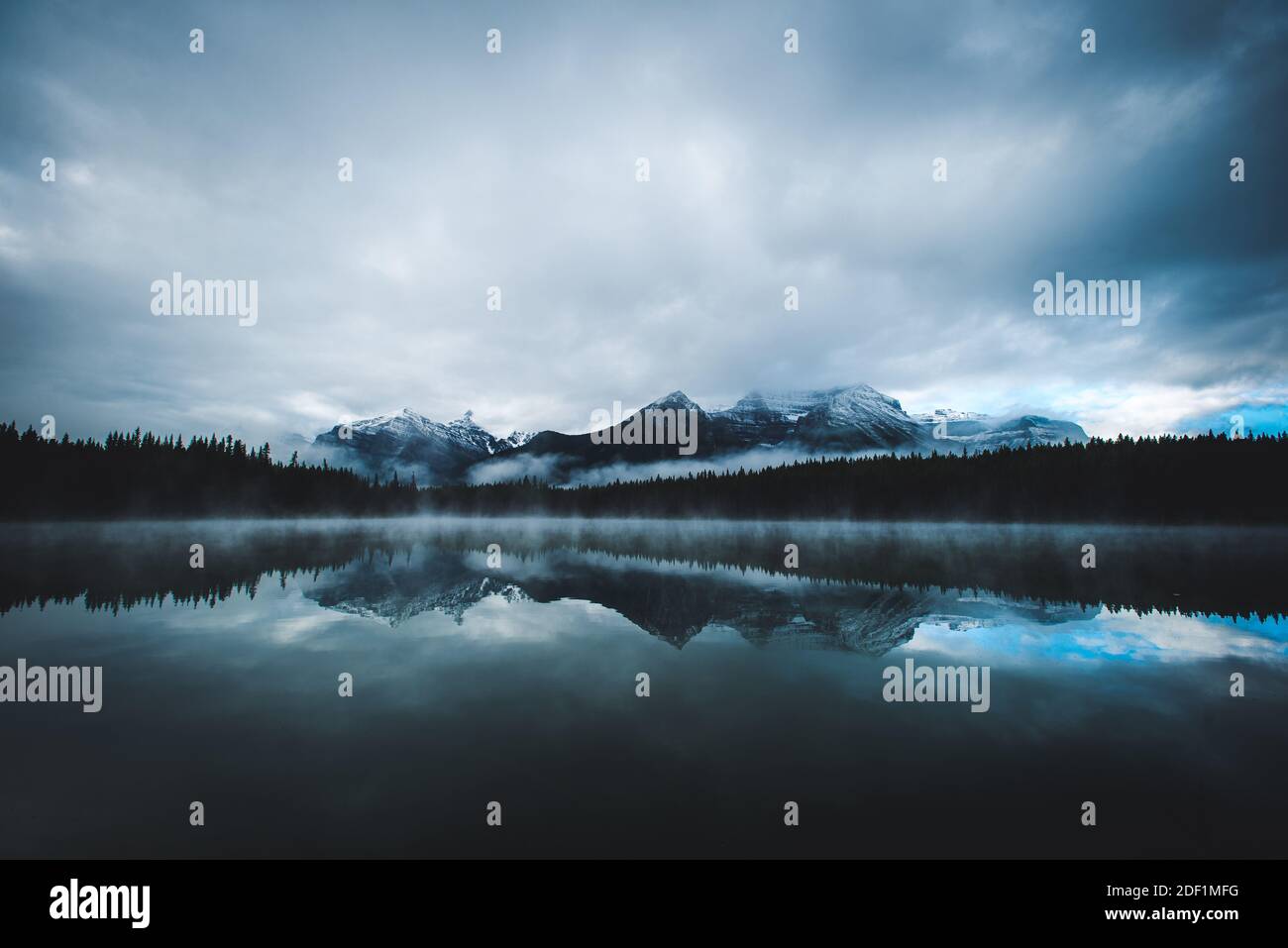 A moody reflection of mountains in Banff National Park on a calm lake ...