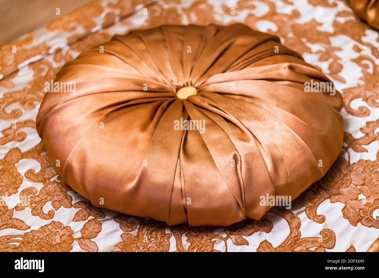 A decorative round-shaped cushion on a fabric with floral patterns ...